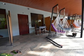 Quarto com teto de madeira, área de jantar com mesa e cadeiras, e espaço com várias redes.