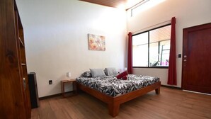 Quarto com cama de madeira, mesa de cabeceira, luminária na parede, janela com cortinas e porta.