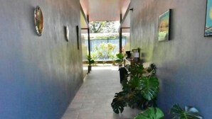 Um corredor com piso ladrilhado, plantas em vasos e quadros nas paredes.