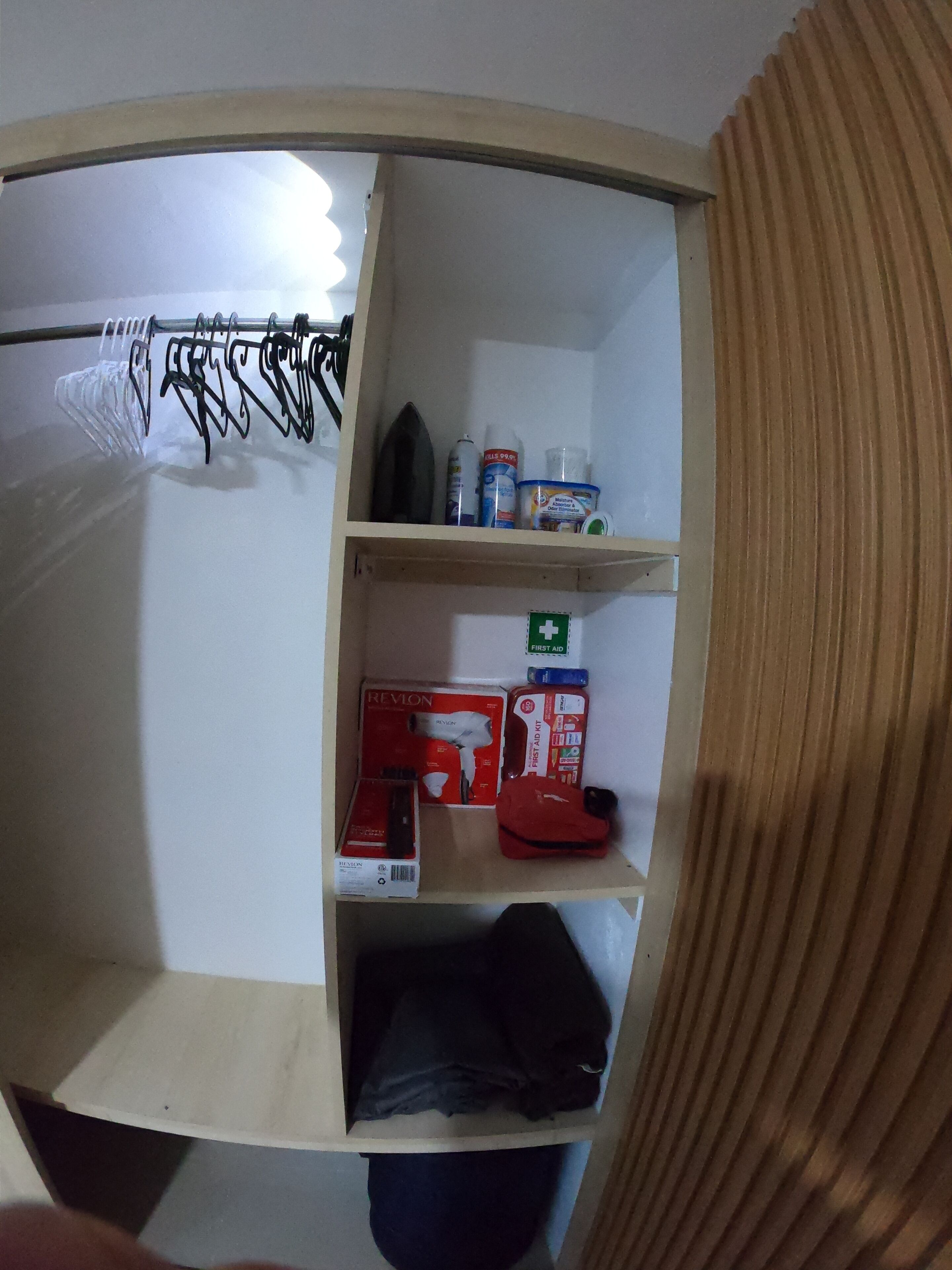 Um espaço de armazenamento com prateleiras contendo diversos itens, incluindo um kit de primeiros socorros, um secador de cabelo e outros produtos de higiene pessoal.