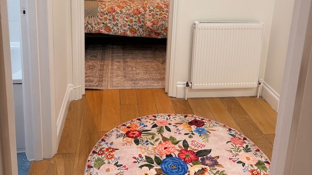 Quarto com uma cama, radiador, tapete floral e um quadro na parede.