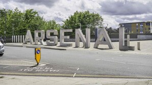 Uma estrada com letras de concreto grandes formando a palavra 'ARSENAL' e uma placa indicativa amarela.