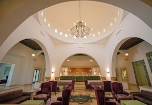 Um hall amplo com tetos arqueados, um lustre central e áreas de estar.