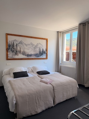 Quarto de hotel com uma cama, um quadro de paisagem de montanhas, uma janela com cortinas e um radiador.