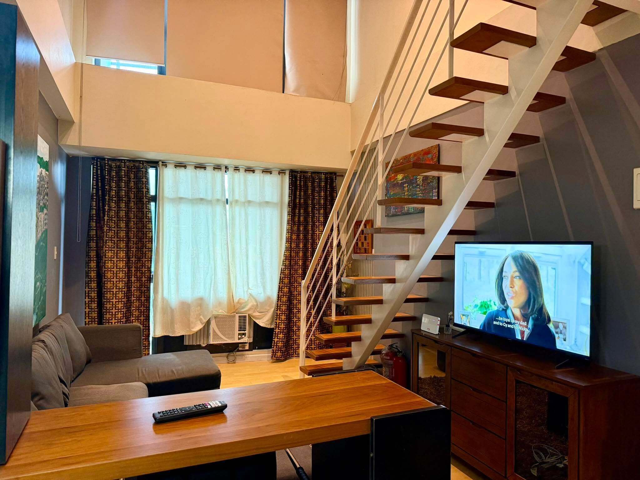 Uma sala de estar moderna com uma mesa de jantar de madeira, um sofá, uma TV e uma escada com corrimão.