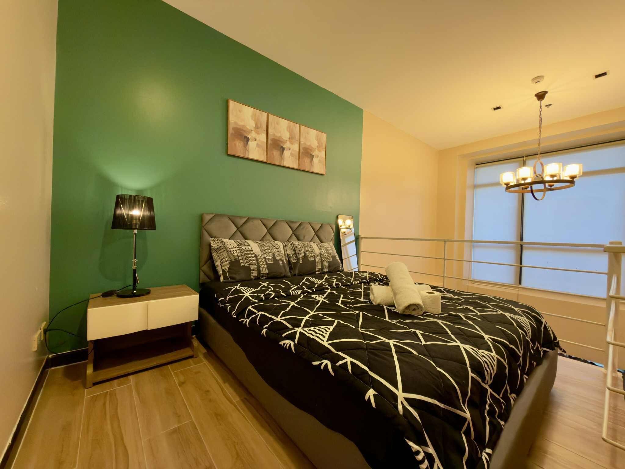 Quarto com cama, mesa de cabeceira, luminária, lustre e janela.