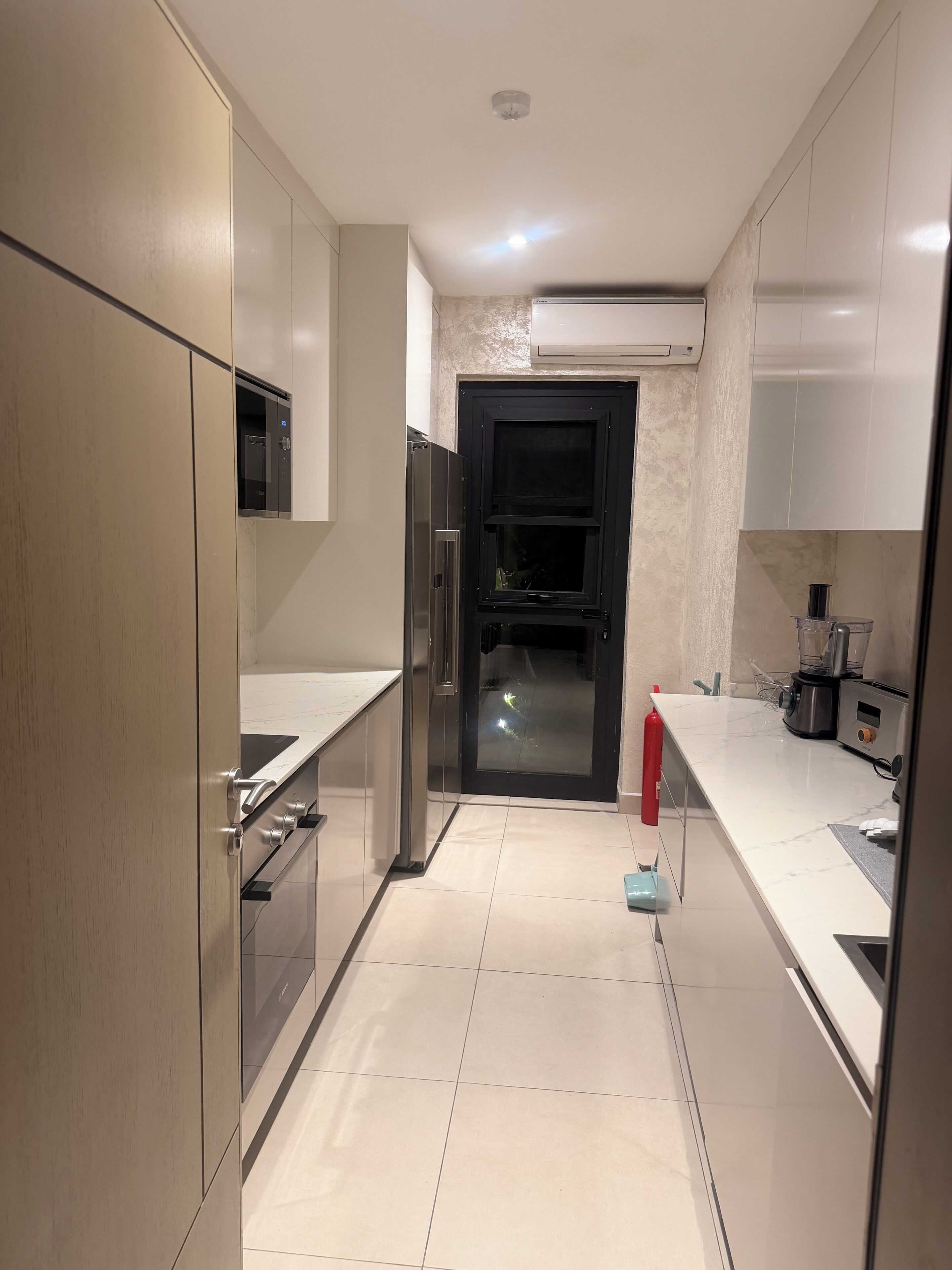 Uma cozinha moderna com eletrodomésticos de aço inoxidável, bancadas brancas e porta com moldura preta.