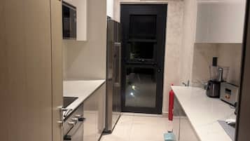 Uma cozinha moderna com eletrodomésticos de aço inoxidável, bancadas brancas e porta com moldura preta.