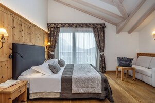 Quarto com cama, mesas de cabeceira, um sofá e uma janela com cortinas.