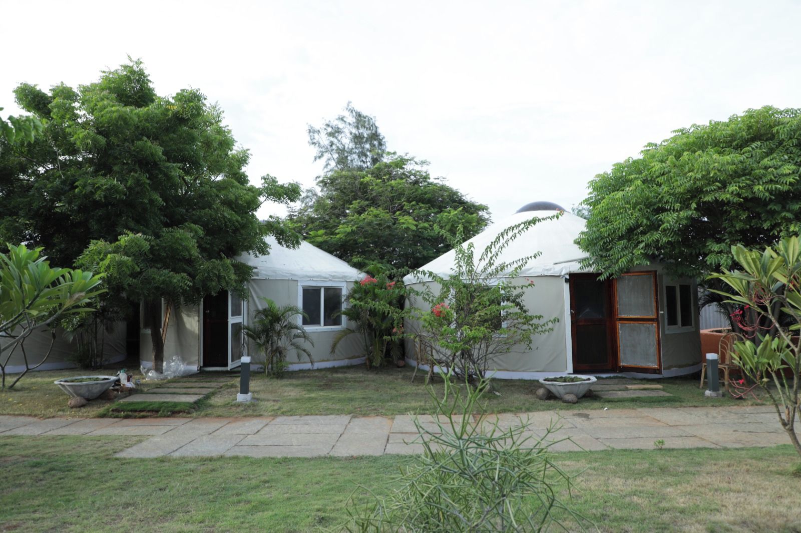 Bairro residencial com duas casas, uma com porta e janela visíveis, e outra com a porta entreaberta. Há árvores e um pequeno jardim com um caminho.