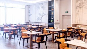 Restaurante com várias mesas e cadeiras, parede com design de bambu e um prateleira com objetos decorativos.