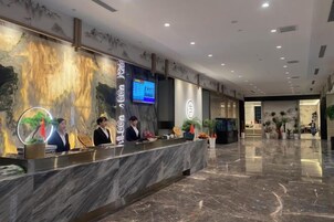 Uma área de recepção de hotel com balcão de mármore, funcionários da recepção, uma tela digital e um grande mural na parede.