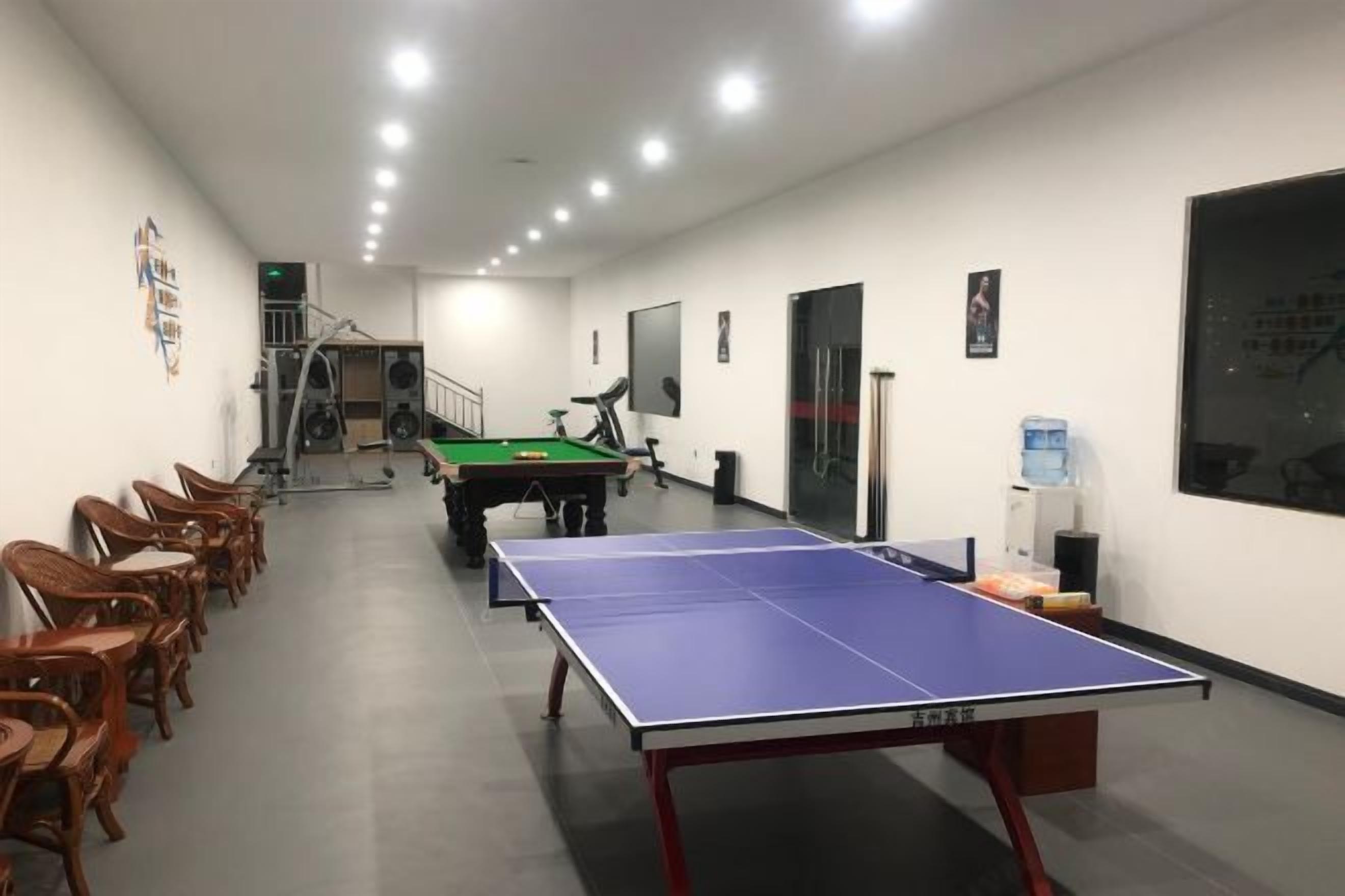 Um quarto com mesa de pingue-pongue, cadeiras, mesa de bilhar e equipamentos de ginástica.