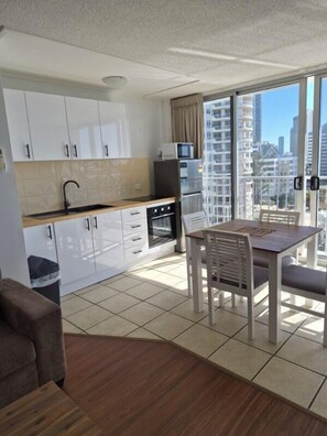 Cozinha moderna com armários brancos, área de refeições com mesa e cadeiras, e vista para a paisagem urbana através de amplas janelas.