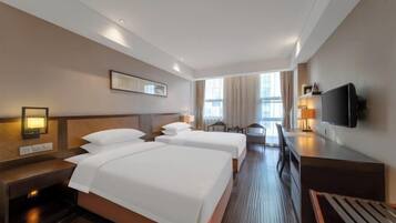 Quarto de hotel com duas camas, uma escrivaninha, uma televisão e uma janela.