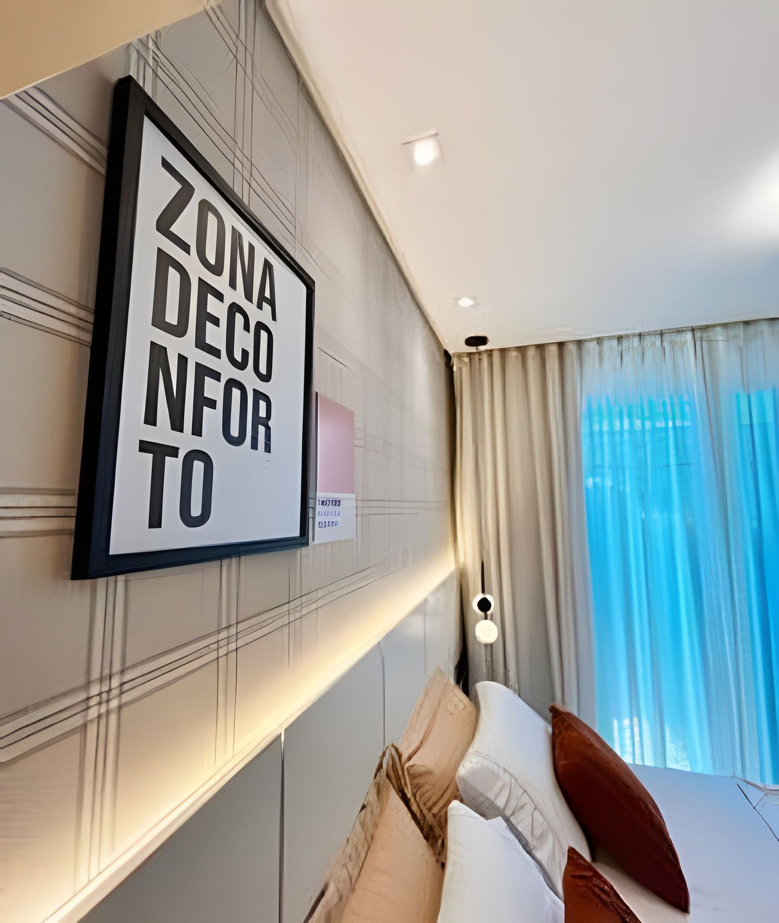 Quarto de hotel com um quadro na parede, uma cama com almofadas, uma mesa de cabeceira e uma janela com cortinas.