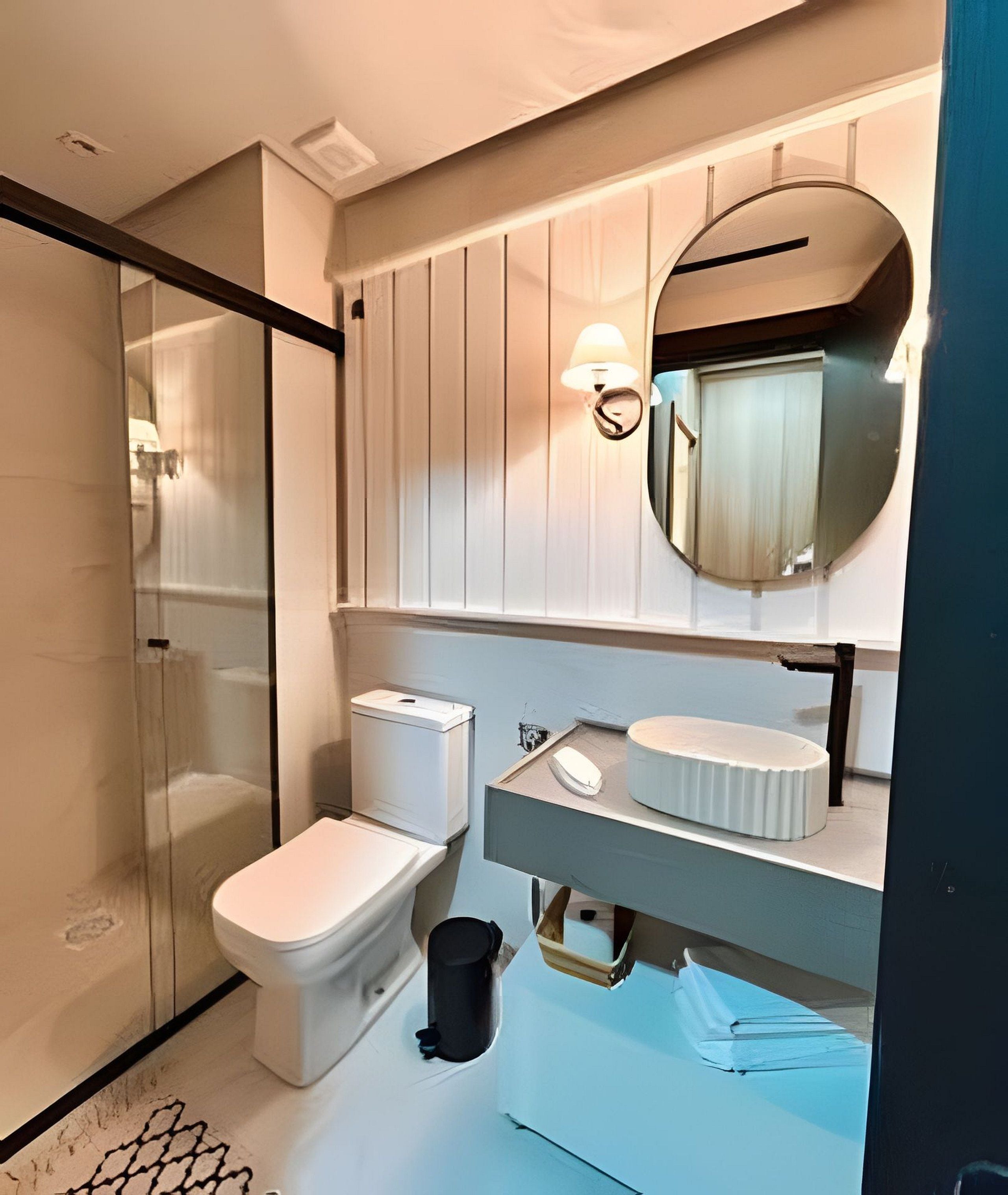 Uma casa de banho moderna com cabine de chuveiro em vidro, sanita, lavatório com espelho e um cesto de lixo.