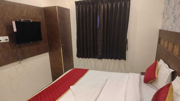 Quarto de hotel com uma cama, televisão na parede e janela com cortinas.