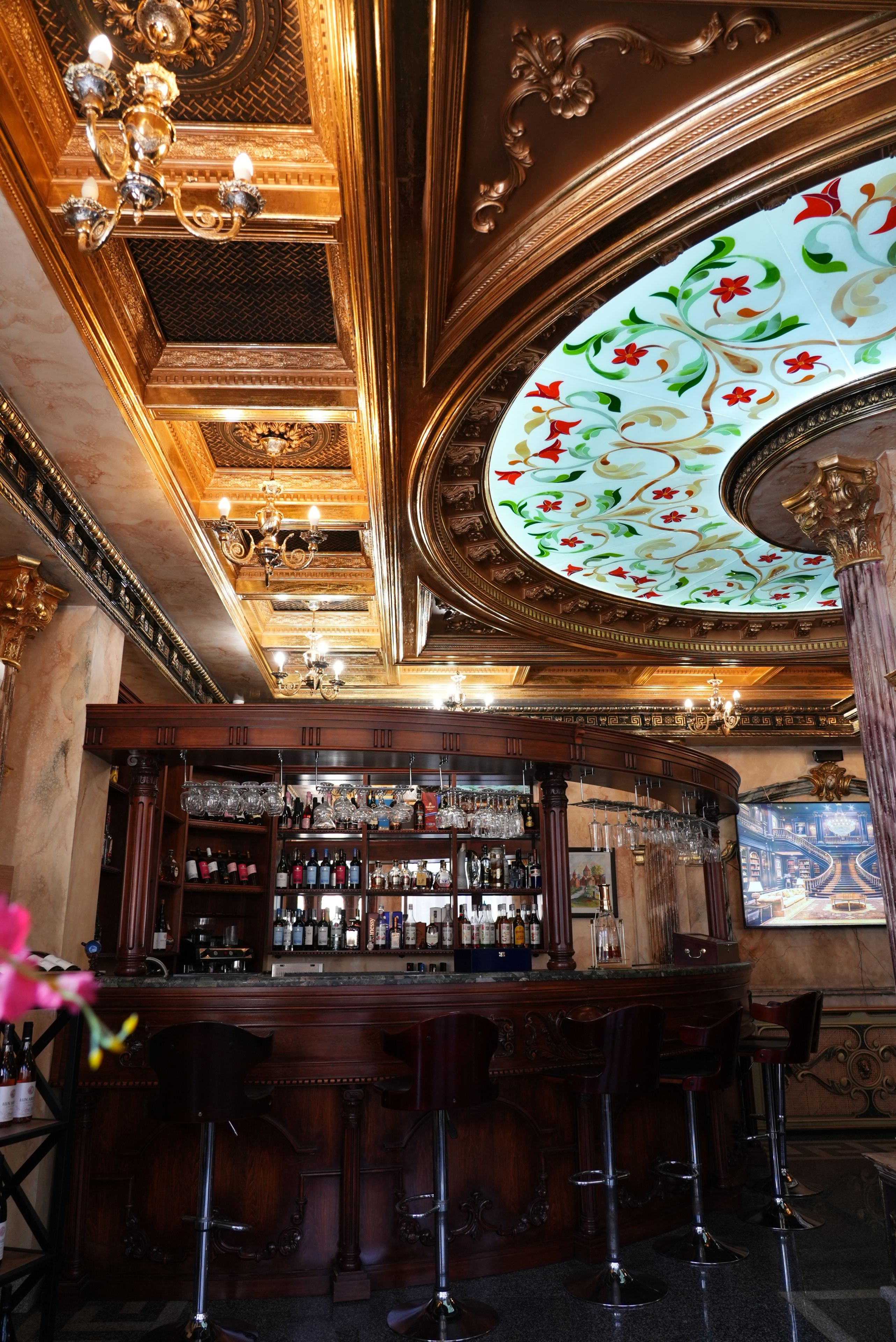 Um espaço de bar luxuoso, com detalhes ornamentais no teto e um teto de vidro decorativo.