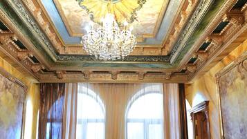 Quarto luxuoso com teto ricamente decorado, um candelabro e mobiliário clássico.