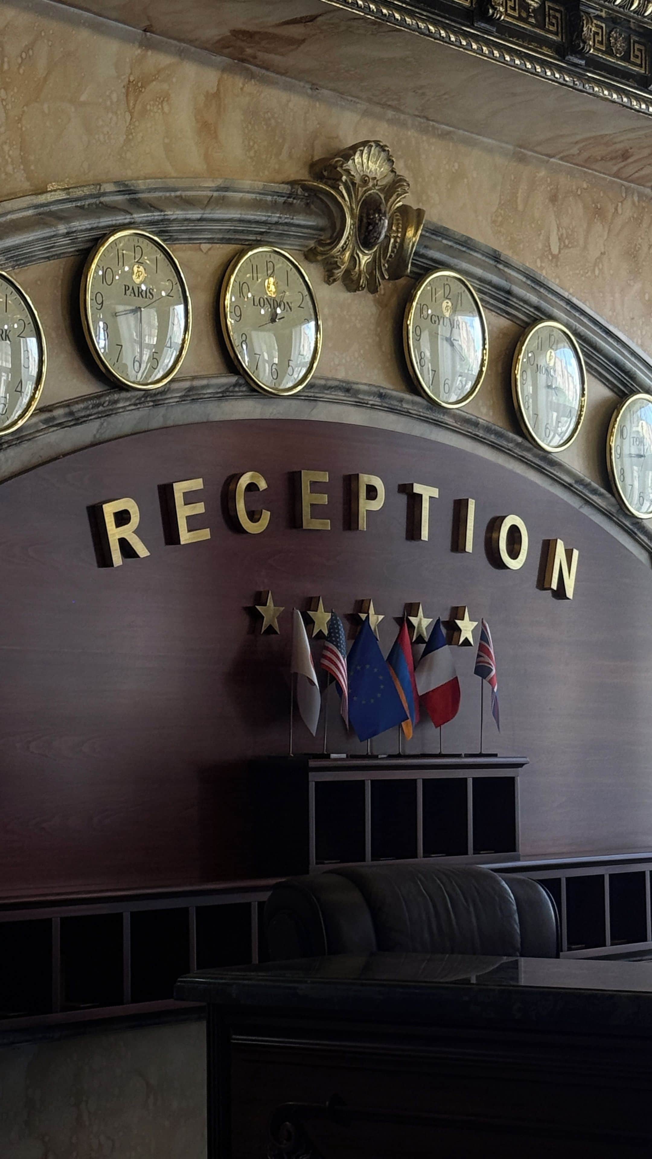 Uma área de recepção com parede de mármore, vários relógios e bandeiras.