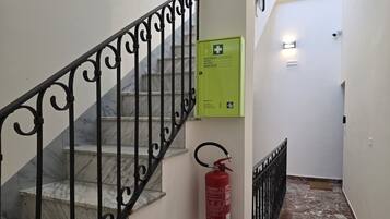 Escada com extintor fixado na parede e placa de saída de emergência verde.