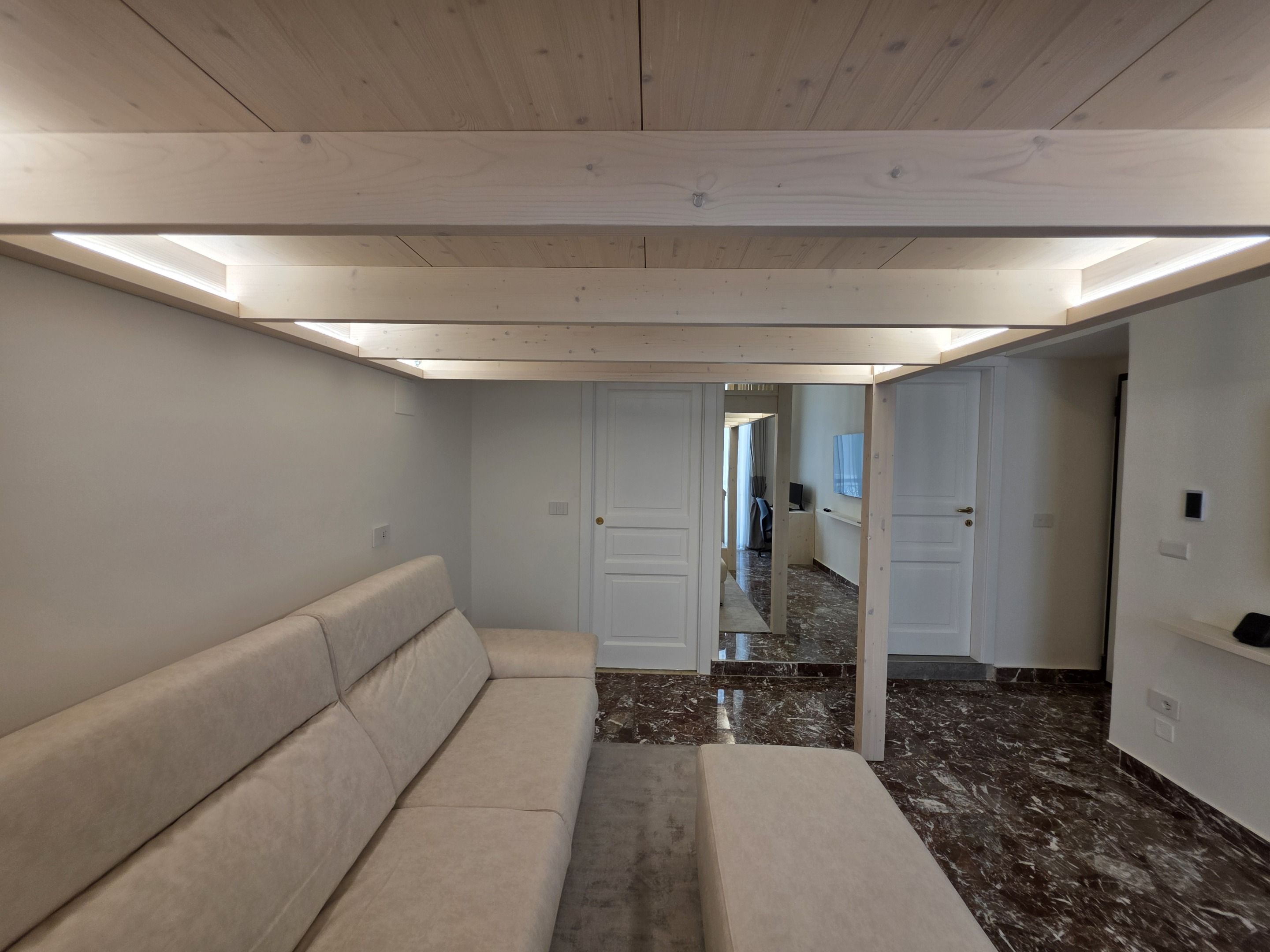 Um corredor com sofá bege, piso de mármore e teto de madeira.