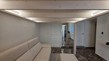 Um corredor com sofá bege, piso de mármore e teto de madeira.
