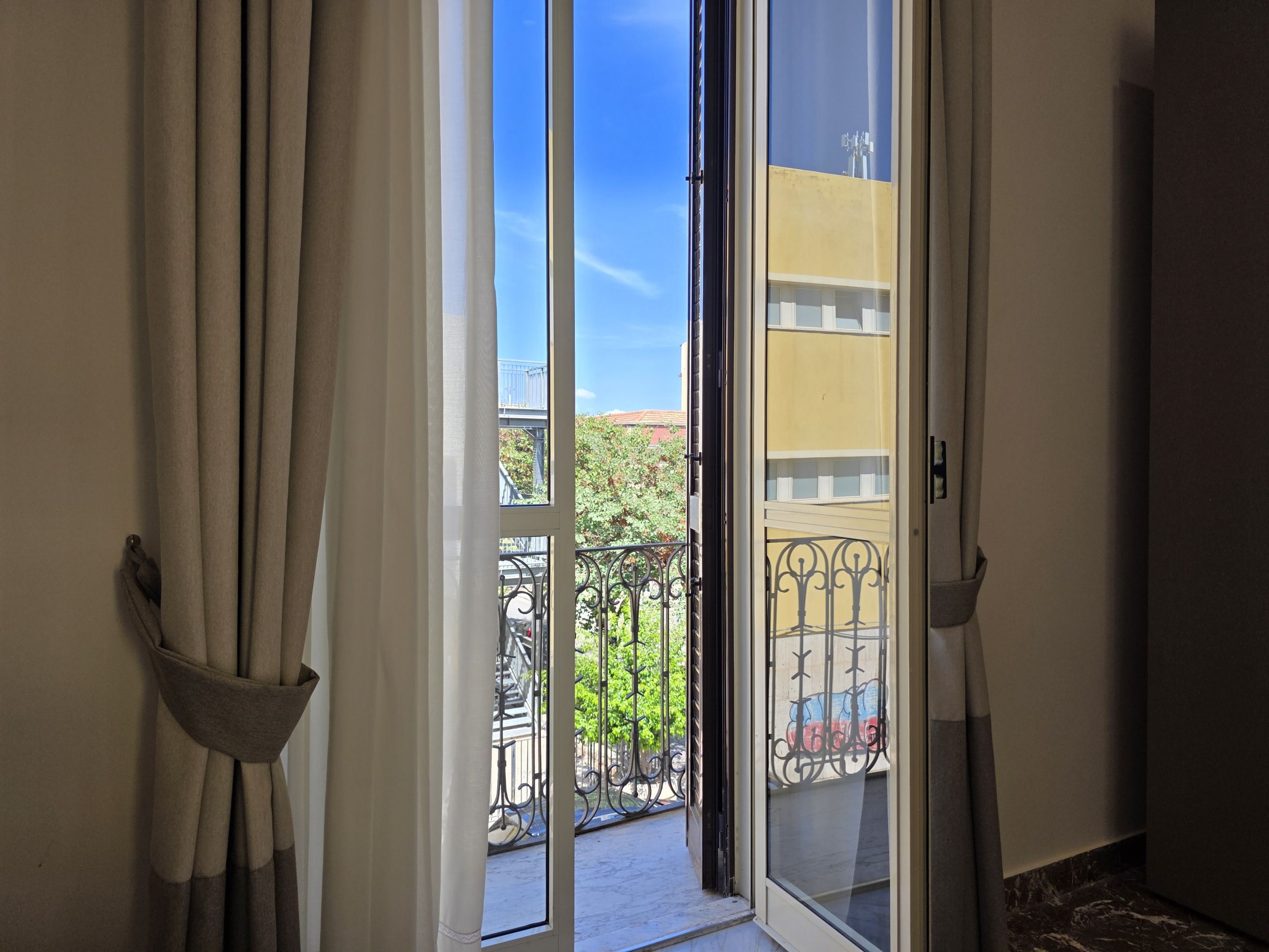 Vista de um quarto com porta de correr de vidro que dá para uma varanda externa com guarda-corpo de metal.