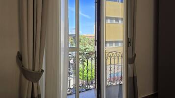 Vista de um quarto com porta de correr de vidro que dá para uma varanda externa com guarda-corpo de metal.