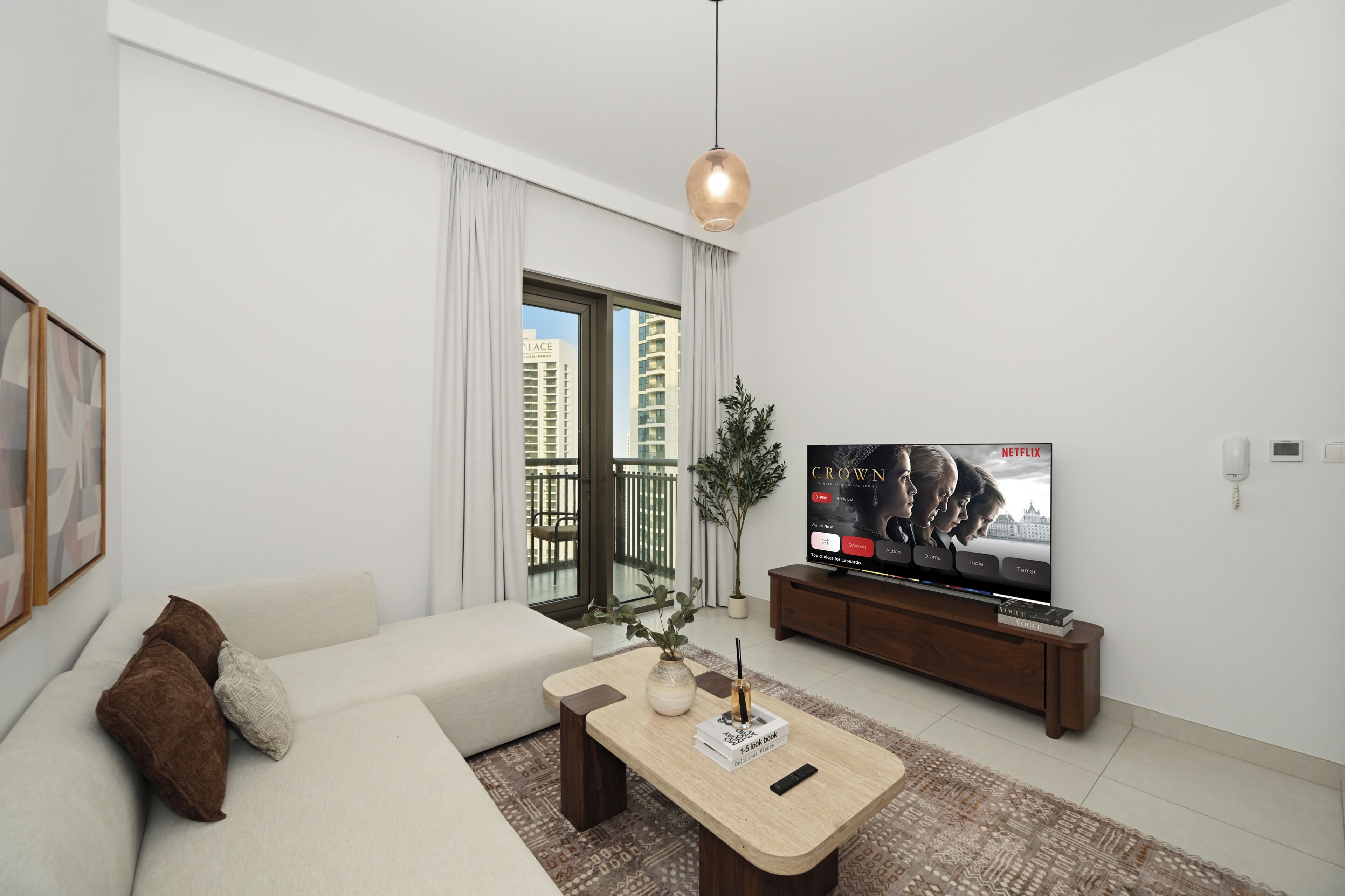 Uma sala de estar moderna com sofá, mesa de centro, televisão e varanda com vista para edifícios altos.