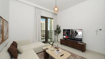Uma sala de estar moderna com sofá, mesa de centro, televisão e varanda com vista para edifícios altos.