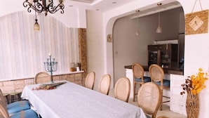 Uma sala de jantar com uma mesa comprida, cadeiras estofadas azuis, cadeiras de vime e um lustre.