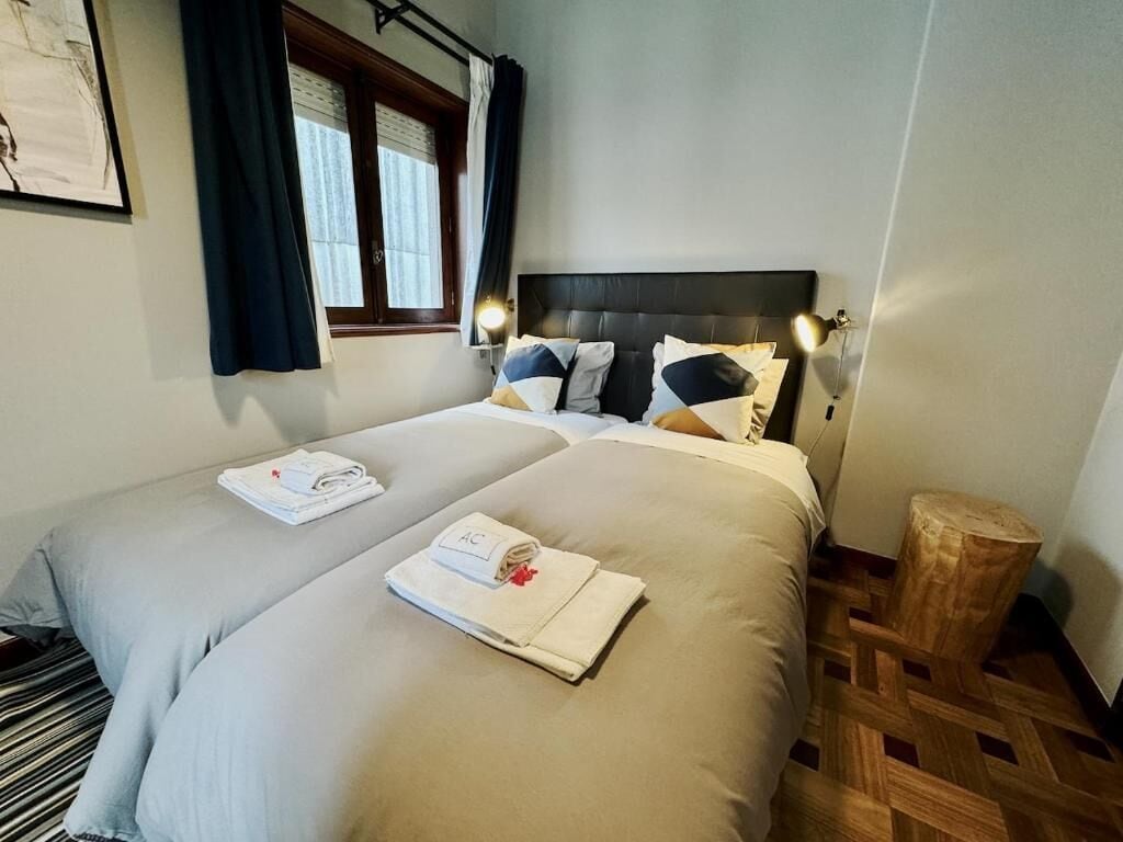 Quarto de hotel com duas camas, chão de madeira e janela com cortinas.