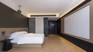 Quarto de hotel moderno com uma cama, mesa de cabeceira, tela de projetor e uma grande tela fixada na parede.