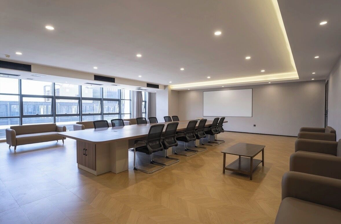 Uma sala de conferências com uma mesa comprida, cadeiras, um sofá e uma tela de projetor.