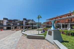Praça pública com fonte, áreas de estar e um edifício com fachada de vidro.