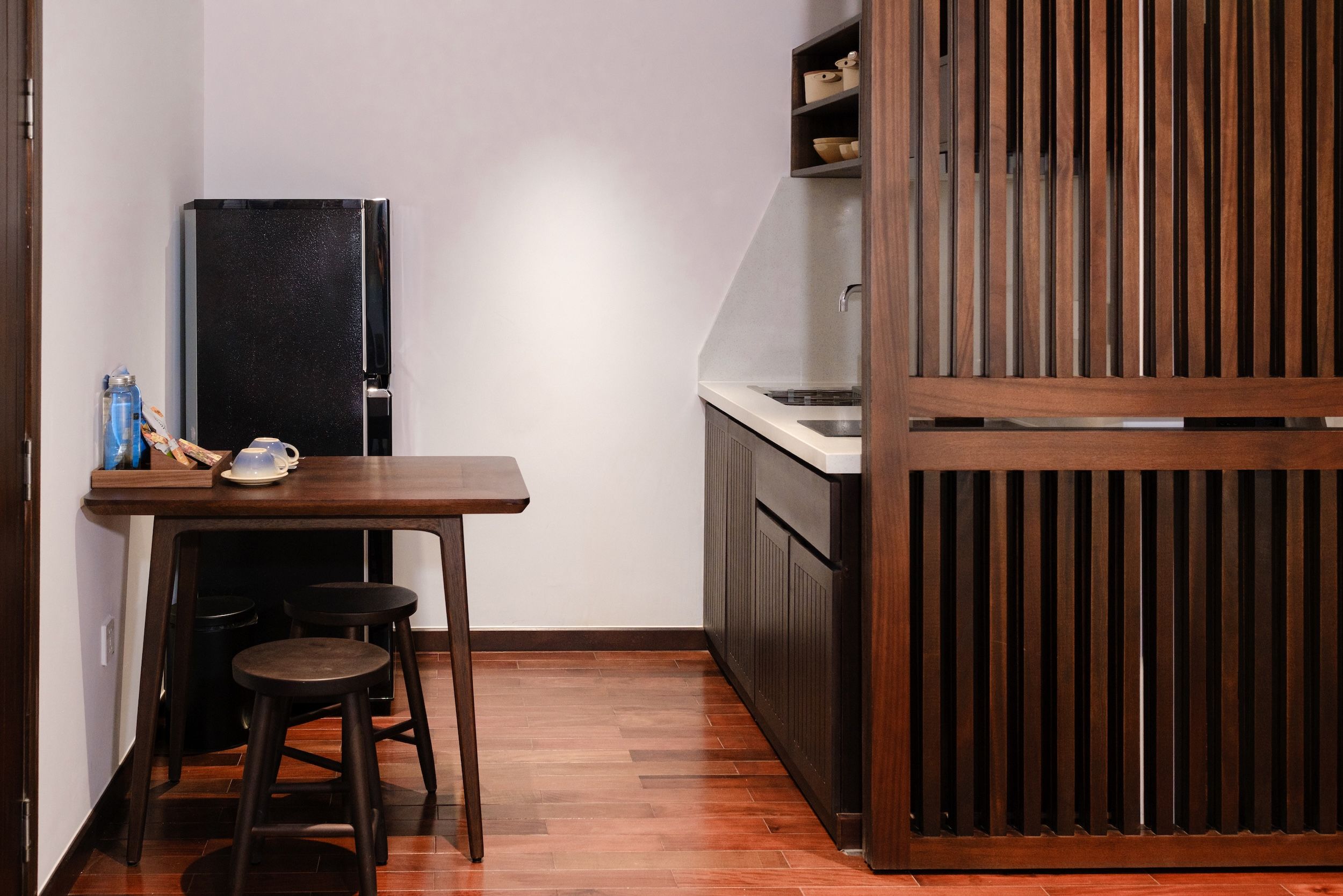Uma cozinha compacta com mesa de madeira, banquetas, geladeira e divisória de madeira.