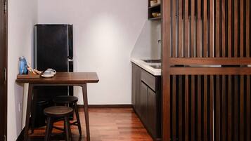 Uma cozinha compacta com mesa de madeira, banquetas, geladeira e divisória de madeira.