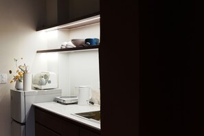 Cozinha moderna com geladeira, micro-ondas e cafeteira no balcão, e uma estante acima com utensílios de cozinha.