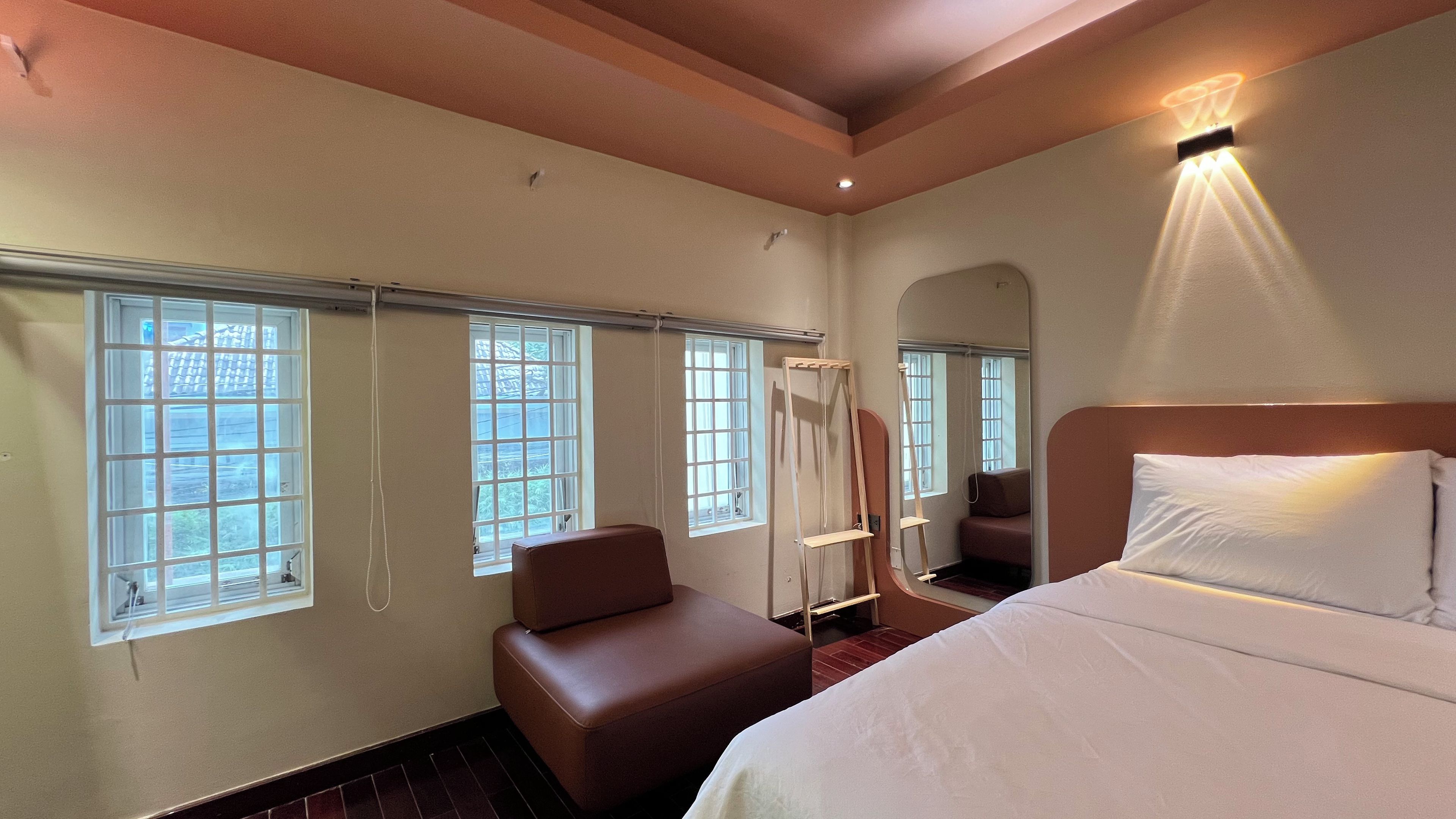 Quarto de hotel com cama, uma cadeira e janela com vista para um edifício.