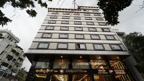 Um hotel de vários andares com fachada moderna, grandes janelas e placas com os dizeres 'AMMAPUR VEG' e 'VYO'.