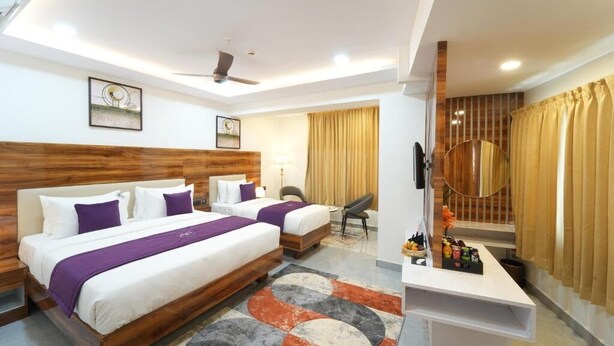 Quarto de hotel com duas camas, uma escrivaninha, uma cadeira e um ventilador de teto.