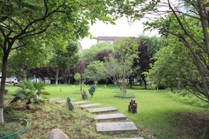 Um jardim com um caminho de pedra, diversas plantas e árvores.