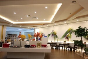Um saguão de hotel com balcão de recepção, área de estar e plantas decorativas.