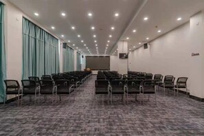 Sala de conferência com fileiras de cadeiras, piso coberto por carpete e tela de projeção.
