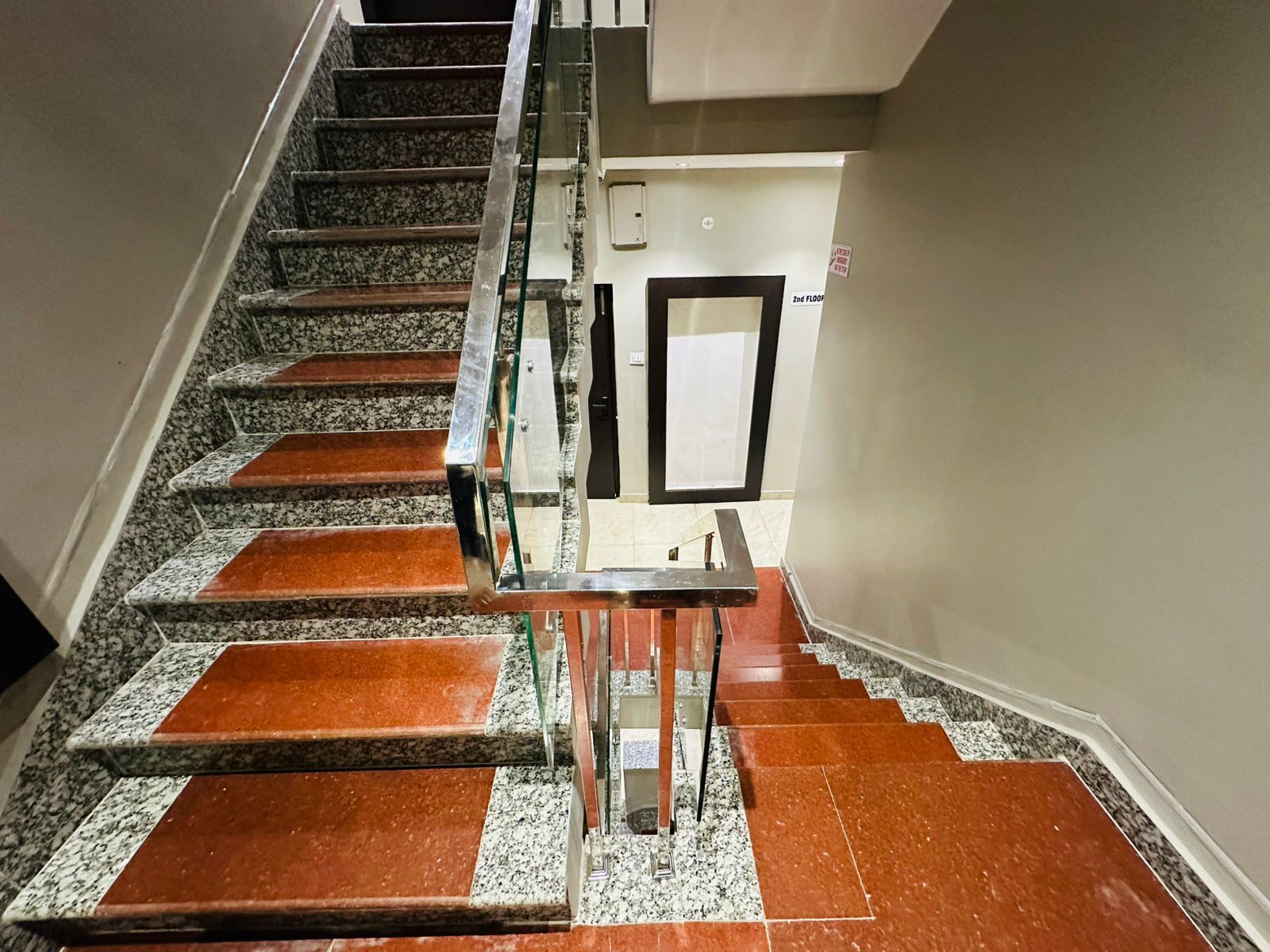 Escadaria com degraus de granito e corrimão de vidro, levando a uma porta com a inscrição '2º ANDAR'.