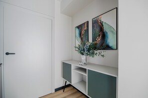 Um corredor com uma porta branca, um console branco com um vaso de flores e duas pinturas abstratas na parede.