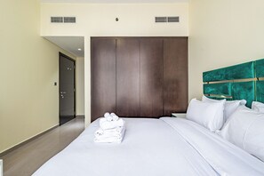 Quarto de hotel com uma cama grande, um guarda-roupa de madeira e uma cabeceira verde-água.