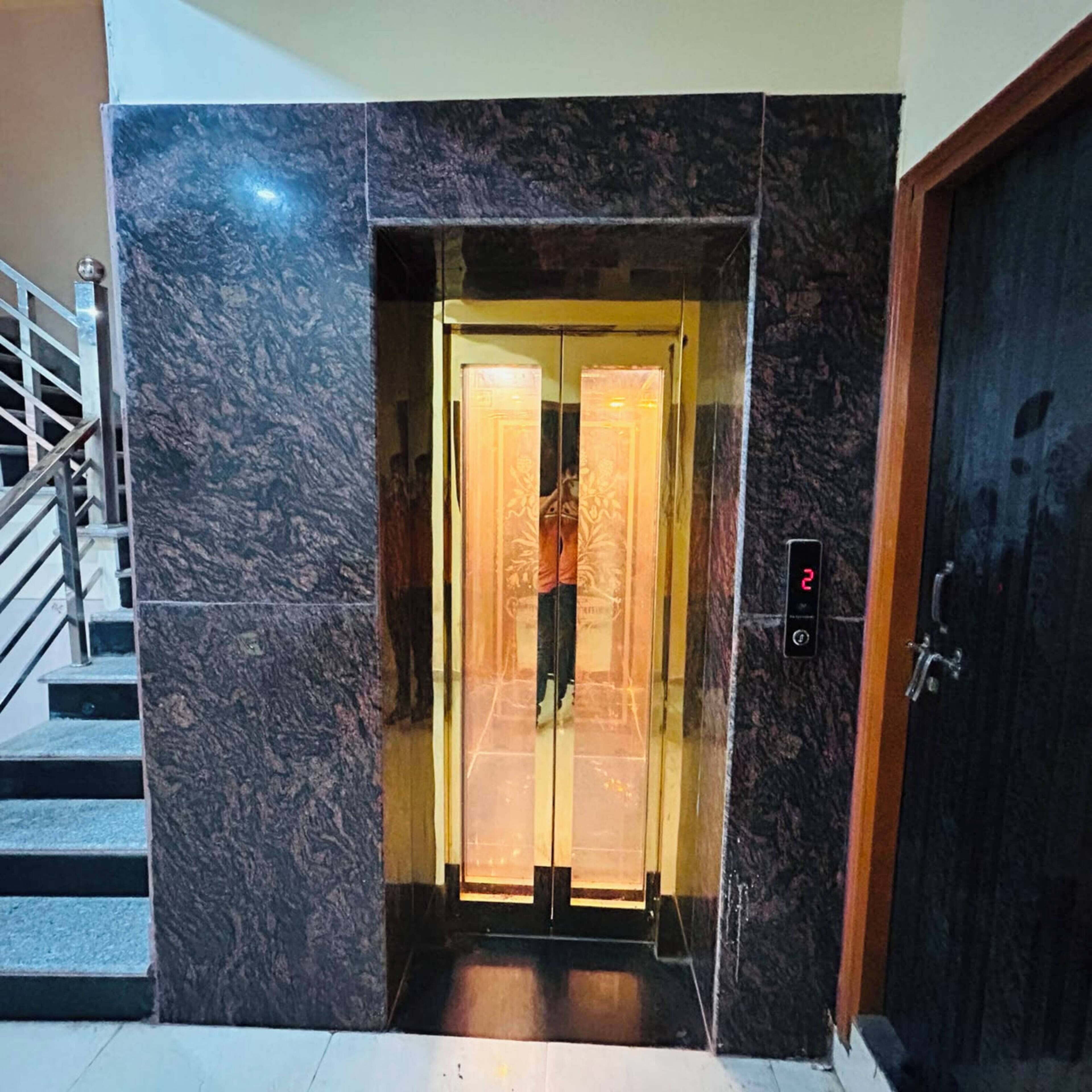 Um elevador com visor digital, uma pessoa no interior e uma escada à esquerda.